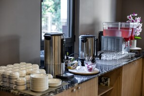 Um espaço com estação de café, diversas máquinas de café, um bebedouro e variedade de xícaras e pratos.