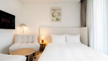 Quarto de hotel com cama, cadeira, mesa pequena, luminária e quadro pendurado na parede.