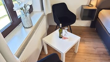 Uma sala de estar moderna com uma cadeira preta, uma mesa branca e uma pequena mesa lateral com uma luminária. Há uma garrafa de vinho e um copo sobre a mesa.