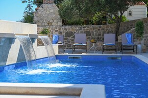 Piscina com cachoeira, paredes de pedra e área de estar externa com guarda-sóis.