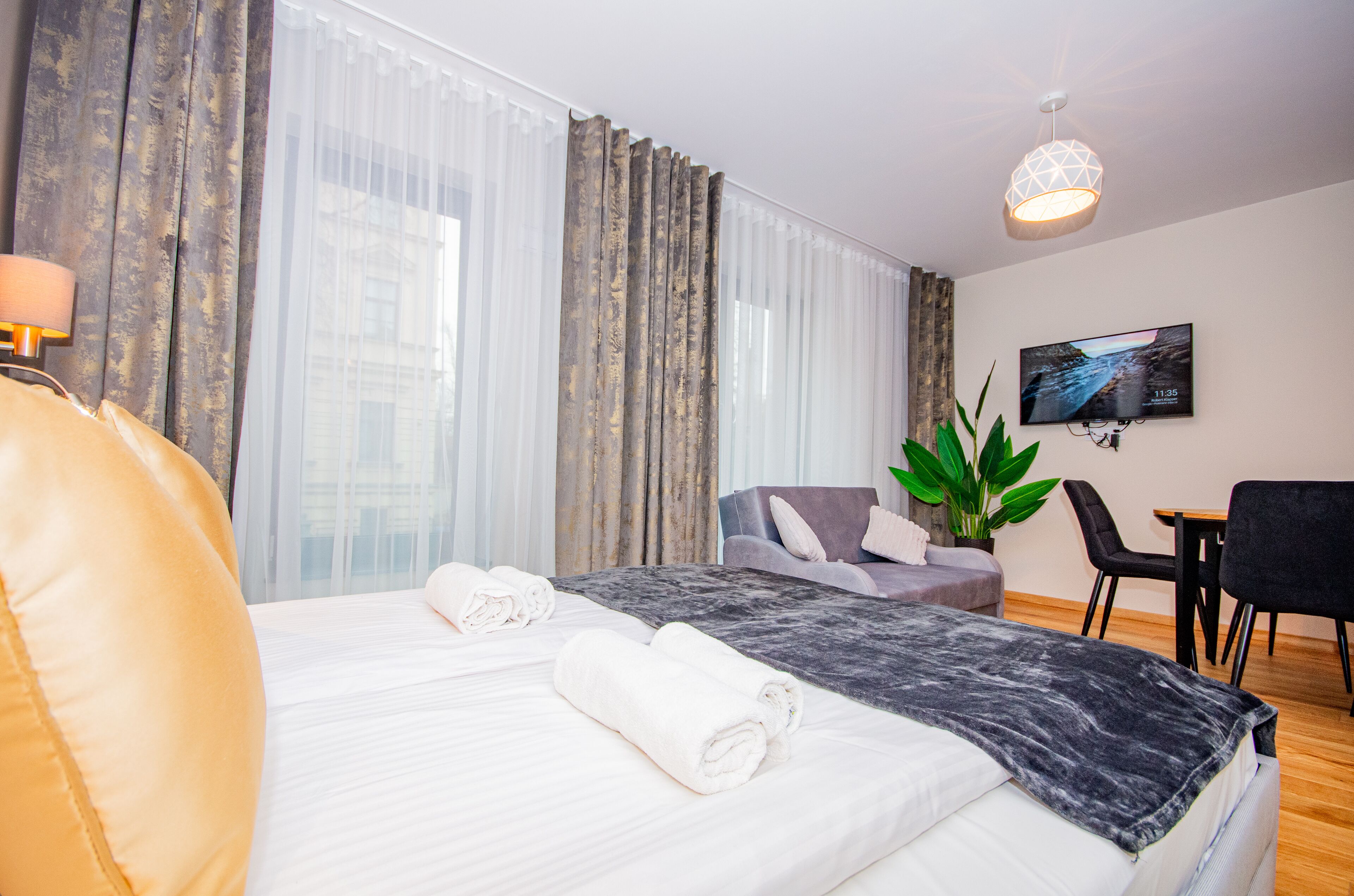 Quarto de hotel com cama, escrivaninha, cadeira, televisão e planta.