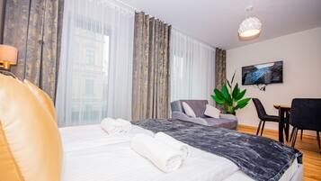 Quarto de hotel com cama, escrivaninha, cadeira, televisão e planta.