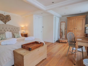 Quarto com cama, mesa de cabeceira, cômoda, espelho e piso de madeira.