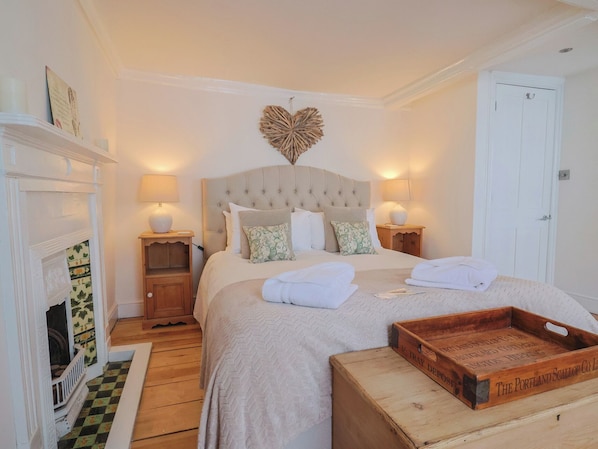 Quarto com cama grande, duas mesas de cabeceira com luminárias, lareira e um banquinho de madeira no chão.