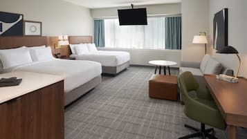 Quarto de hotel com duas camas, uma escrivaninha, uma cadeira, uma televisão e uma janela com cortinas.