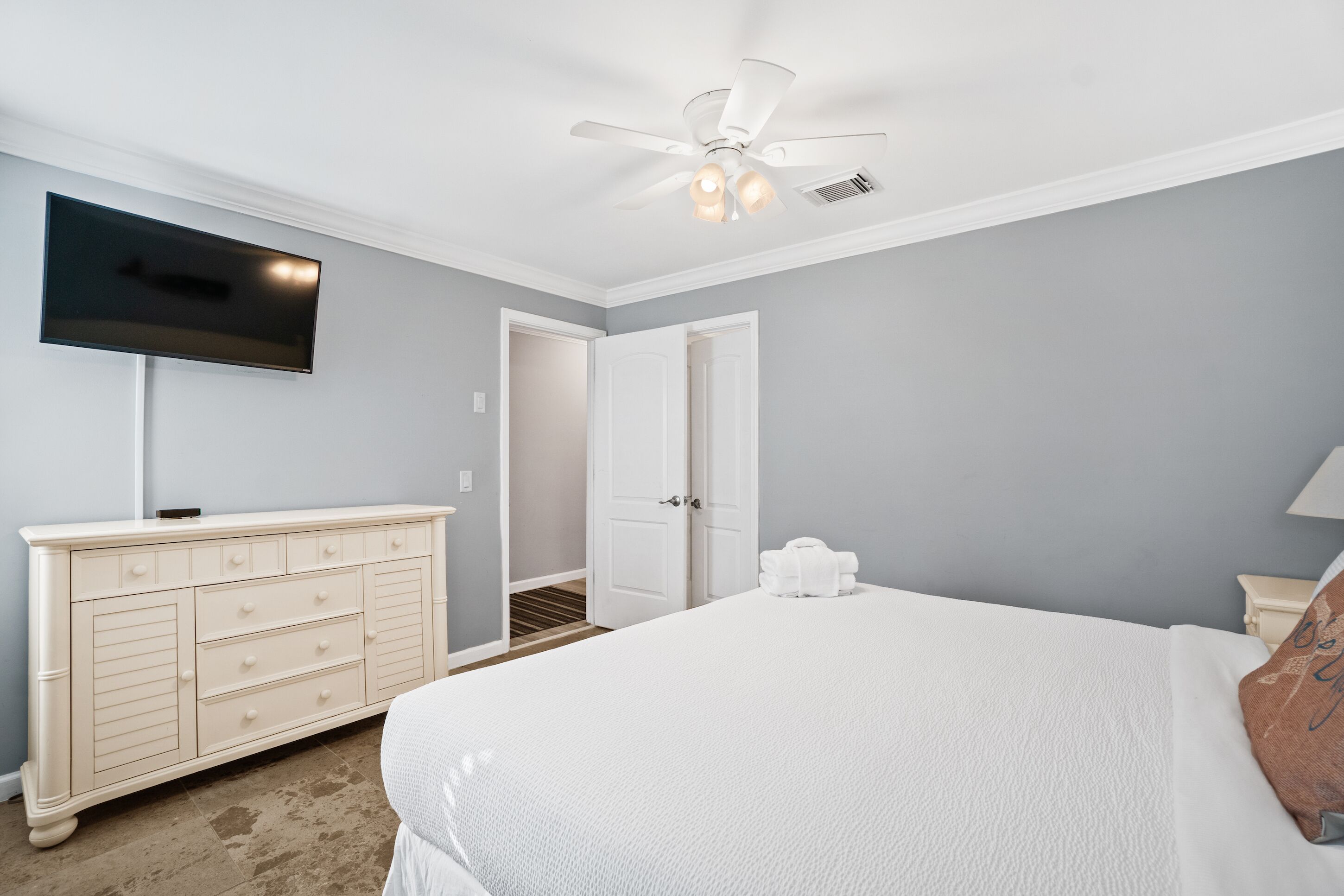 Quarto com cama, penteadeira, televisão na parede e ventilador de teto.