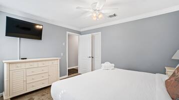 Quarto com cama, penteadeira, televisão na parede e ventilador de teto.