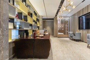 Interior moderno com balcão de recepção em mármore, TV na parede e área de estar com um armário de madeira e luminária pendente.