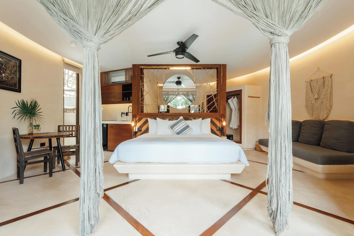 Quarto com cama, ventilador de teto, espelho grande e área de jantar com mesa e cadeiras.