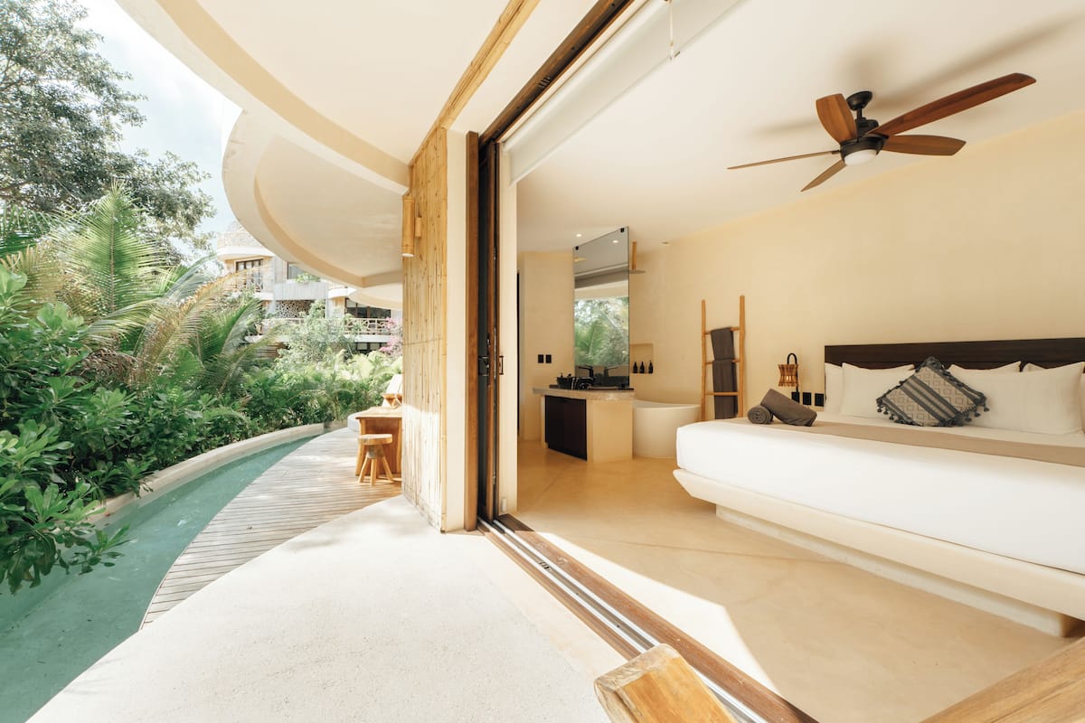 Quarto moderno com uma cama grande, ventilador de teto e vista para a piscina e jardim.