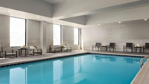Piscina com espreguiçadeiras e mesas, janelas amplas e parede revestida em azulejos.