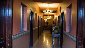 Corredor de hotel com lustre, portas e uma mesa com flores.