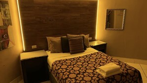 Quarto de hotel com cabeceira de madeira, colcha estampada e toalha dobrada na cama.