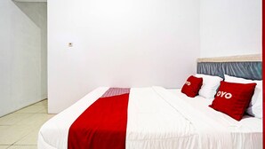 Uma cama bem arrumada com colcha vermelha e branca, duas almofadas vermelhas com a palavra 