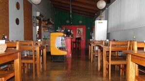 Restaurante com mesas e cadeiras de madeira, um refrigerador amarelo e uma parede verde.