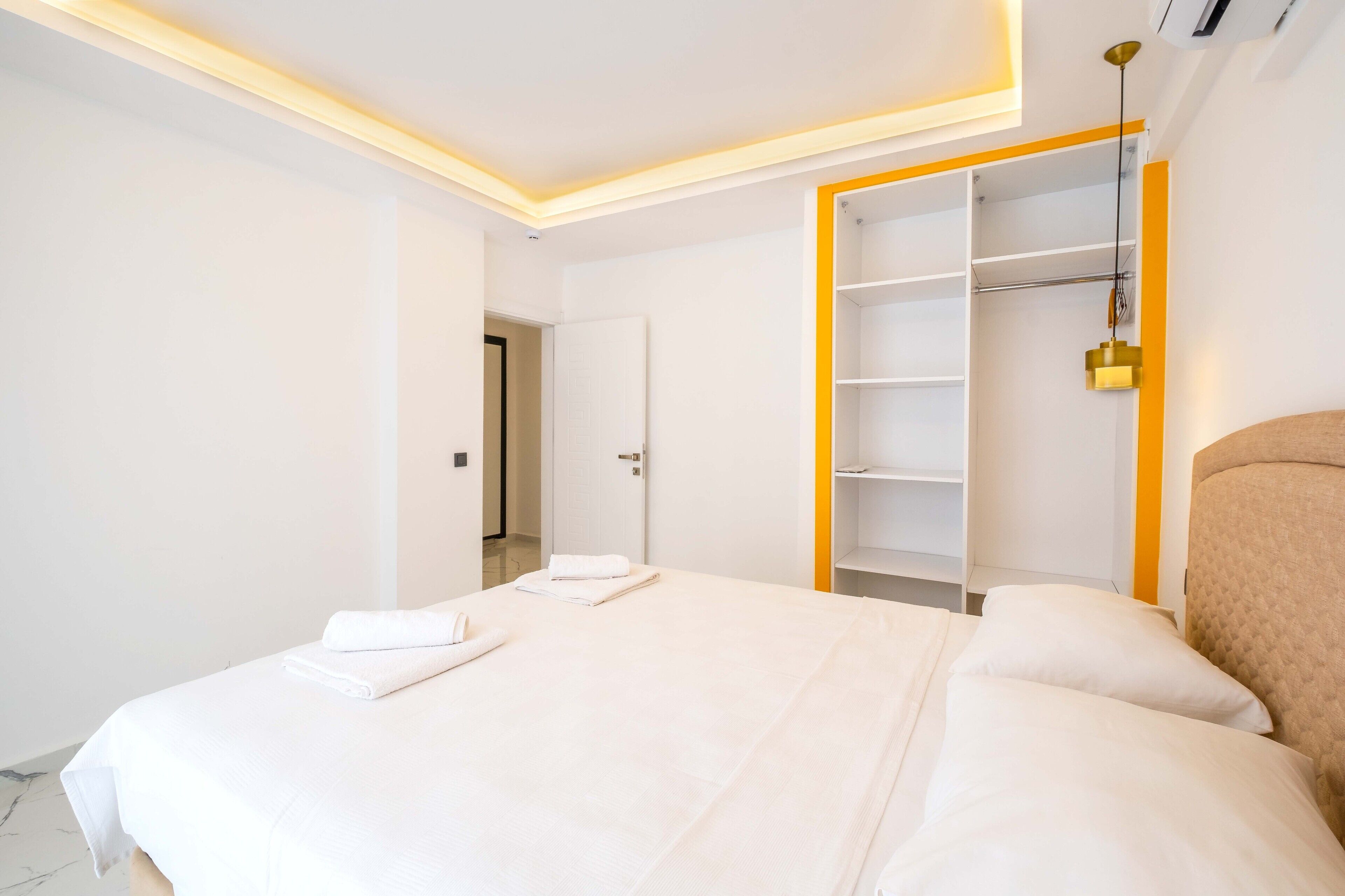 Quarto de hotel com cama arrumada, guarda-roupa com detalhe amarelo e porta que dá para outro cômodo.