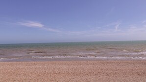 Uma praia com areal pedregoso e mar calmo sob um céu claro.