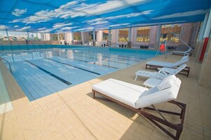 Piscina interna com várias pistas, espreguiçadeiras e área coberta.