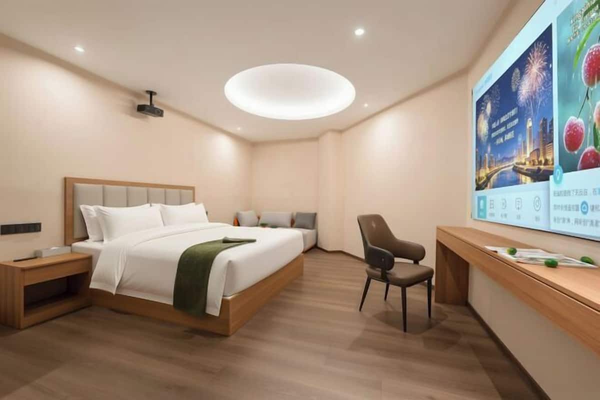 Quarto de hotel com cama, escrivaninha, cadeira e uma janela grande com vista.