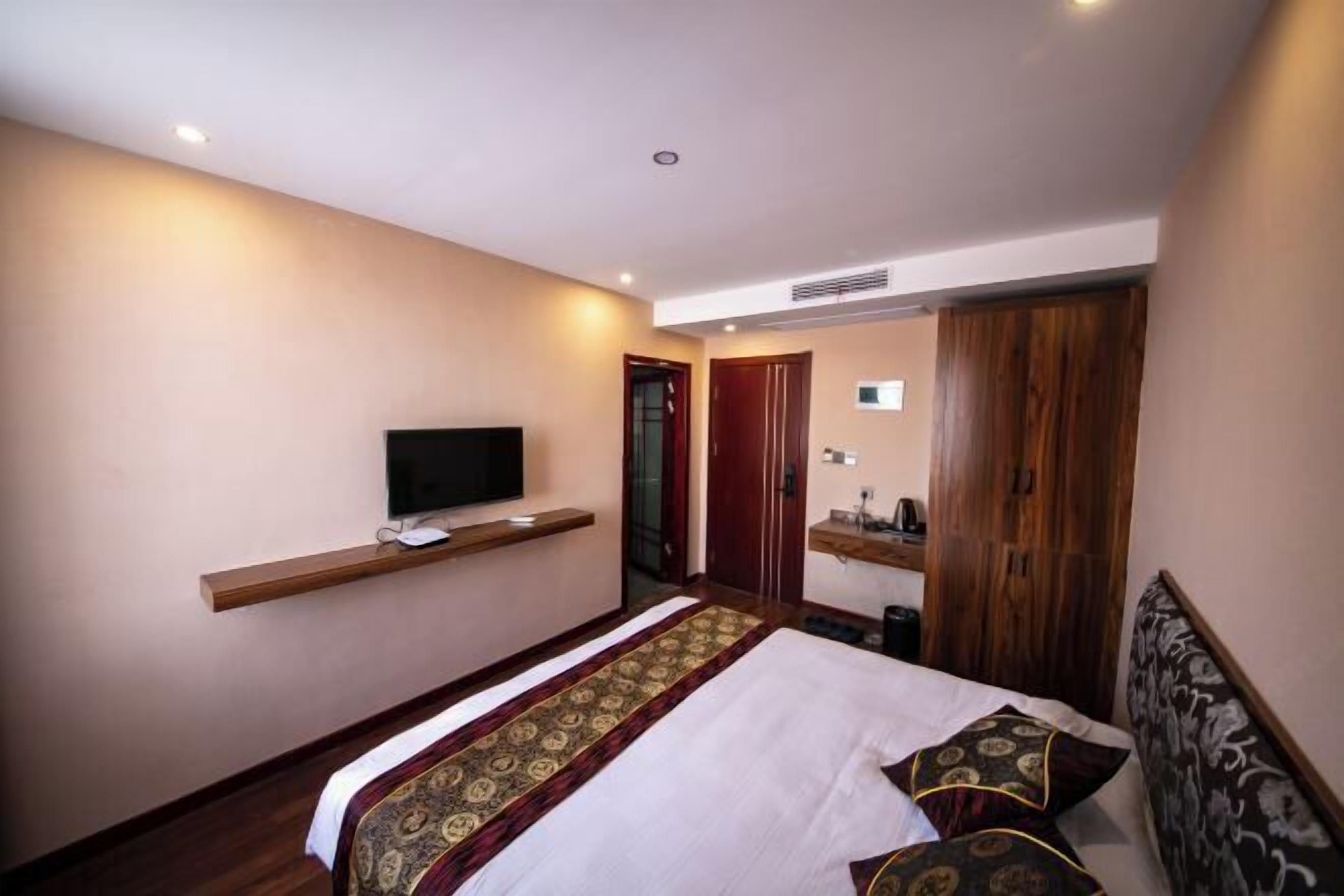 Quarto de hotel com uma cama, televisão fixada na parede, guarda-roupa de madeira e um espelho.