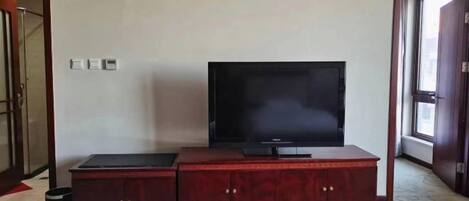 Quarto com televisão sobre um armário de madeira, uma porta e uma janela.