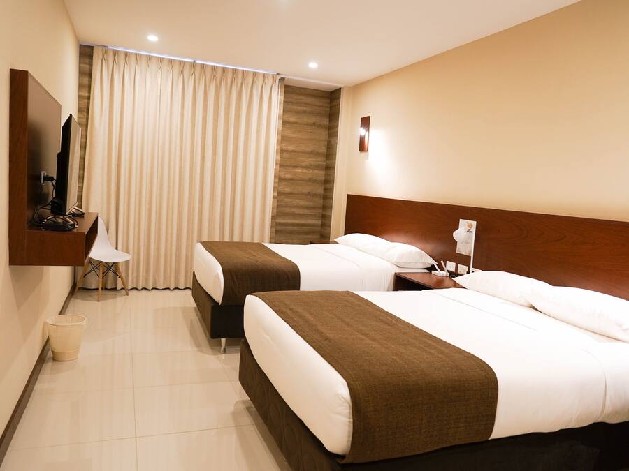 Quarto de hotel com duas camas, televisão, escrivaninha e banheiro.