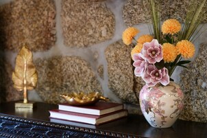 Um vaso com flores e livros sobre uma mesa em frente a uma parede de pedra.