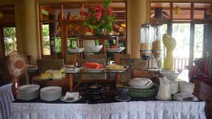 Disposição de buffet com diversos alimentos, um ventilador e um vaso de flores.