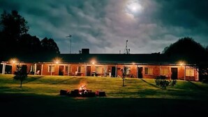 Um motel com uma fileira de quartos, uma fogueira no quintal e uma grande lua no céu.