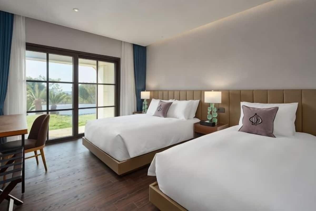 Quarto de hotel com duas camas, uma mesa e vista para o exterior.