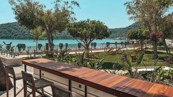 Um deck de madeira com cadeiras e uma mesa com vista para um lago, rodeado por árvores e vegetação.
