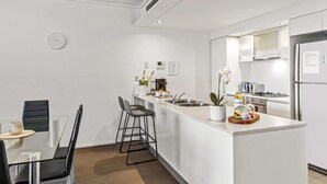 Uma cozinha moderna com ilha central, banquetas de bar e área de refeições com mesa de vidro e cadeiras.