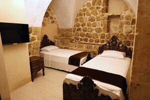 Quarto com duas camas, televisão e paredes de pedra.
