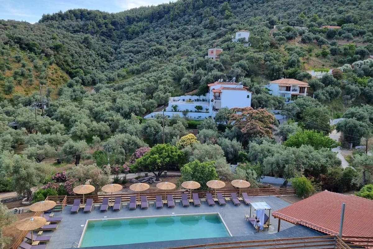 Uma área de piscina com espreguiçadeiras e guarda-sóis, cercada por vegetação exuberante e colinas.