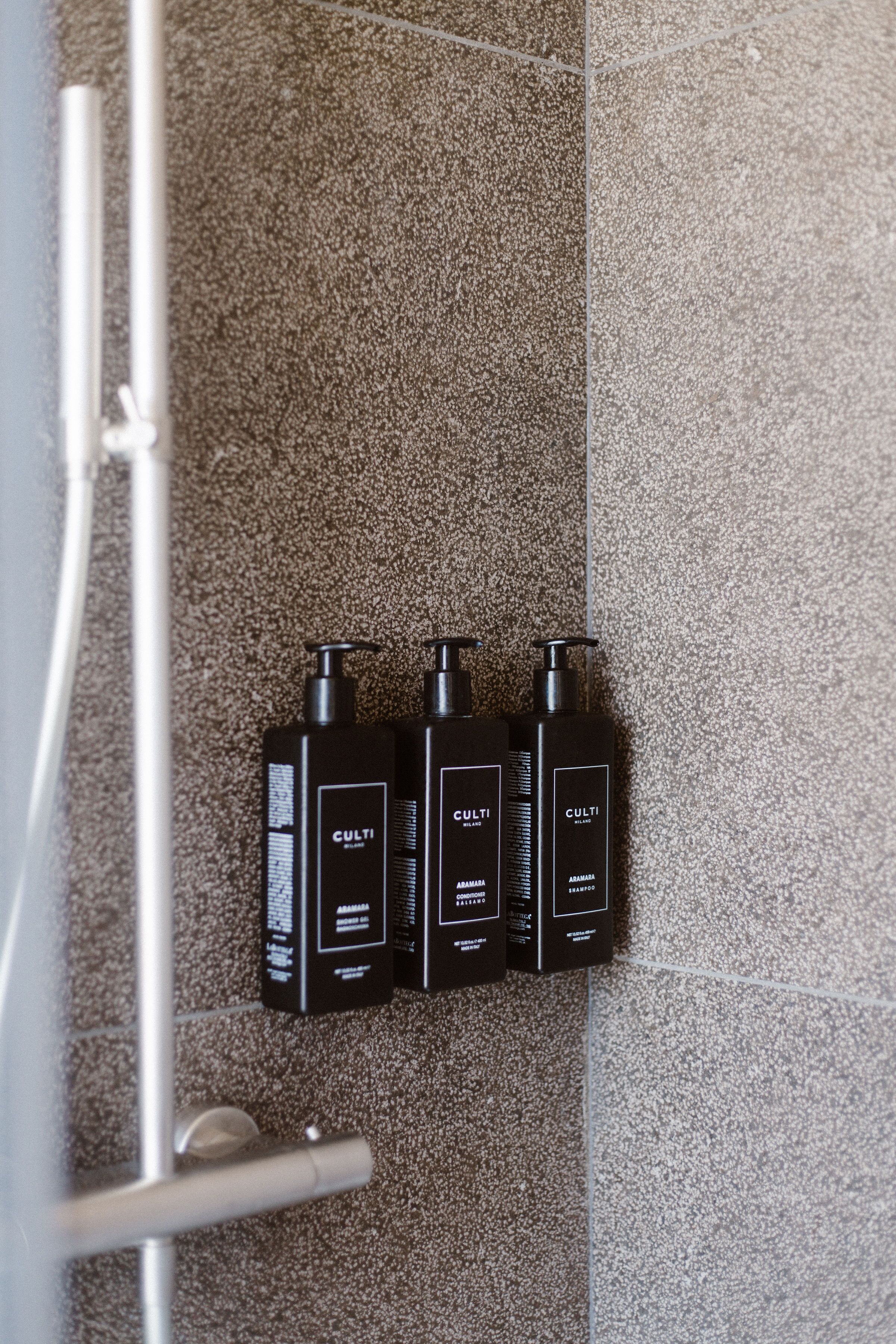 Três frascos pretos de shampoo Culti sobre uma parede texturizada.