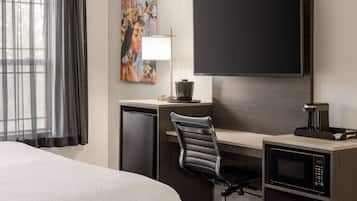 Quarto de hotel com cama, escrivaninha, cadeira, televisão e micro-ondas.