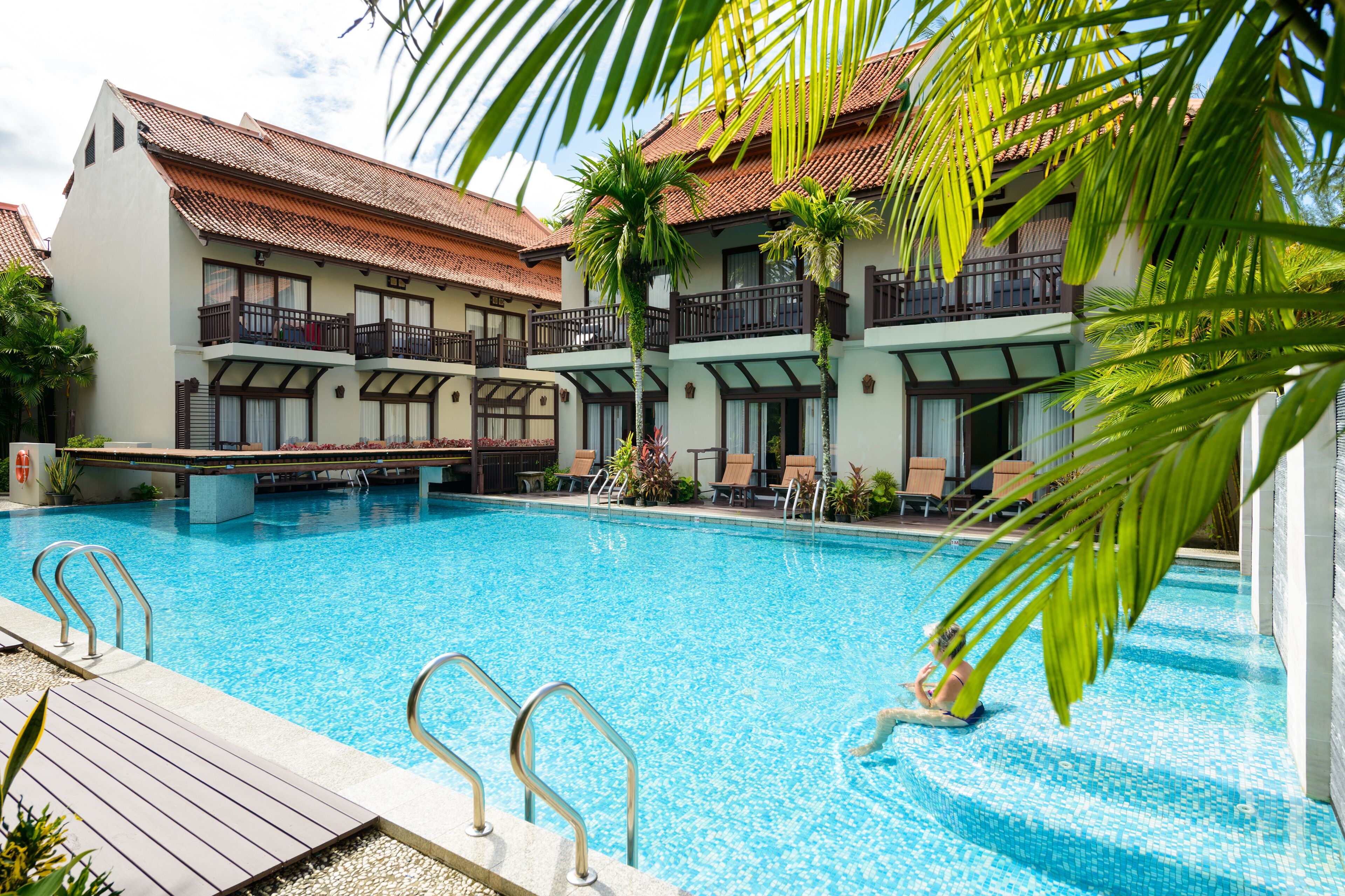Piscina com deck de madeira, rodeada por espreguiçadeiras e palmeiras.