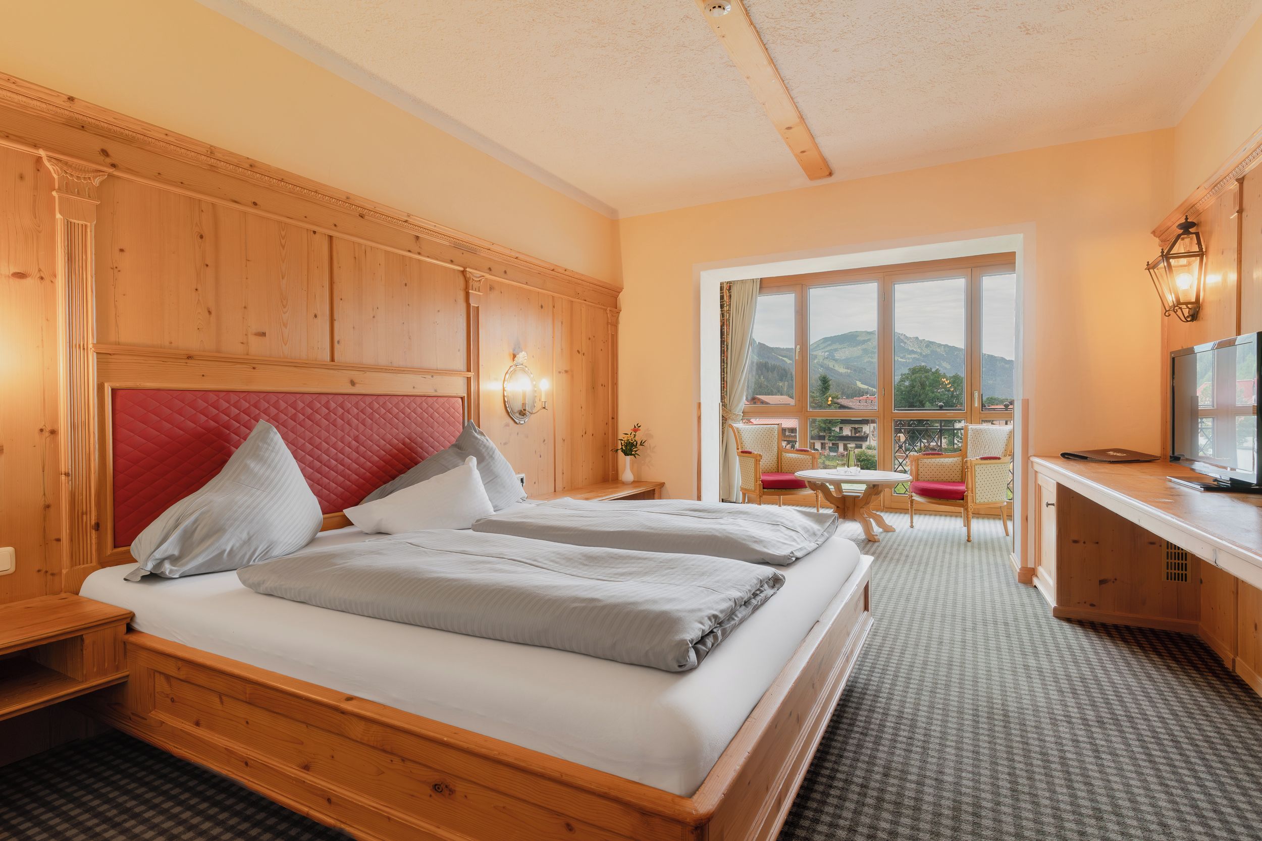 Quarto de hotel com cama, escrivaninha, cadeira e vista para as montanhas.