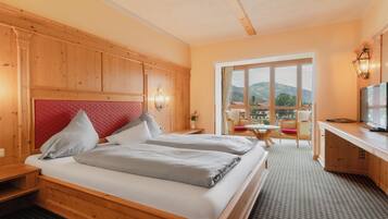 Quarto de hotel com cama, escrivaninha, cadeira e vista para as montanhas.