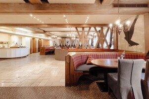 Interior de restaurante com vigas de madeira, área de estar central com uma mesa redonda e um balcão com buffet.