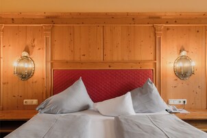 Quarto de hotel com parede de madeira, cabeceira vermelha, duas luminárias de cabeceira e cama com roupa de cama branca e vários travesseiros.