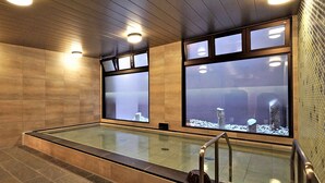 Piscina interior moderna com paredes de vidro transparente, teto de painéis de madeira e chão ladrilhado.