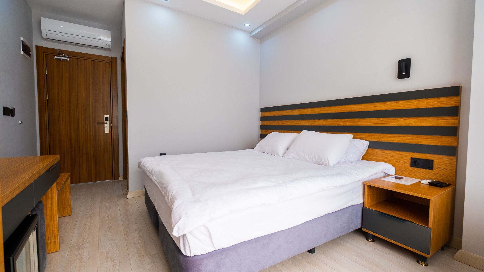 Quarto de hotel com cama, mesa de cabeceira e escrivaninha.