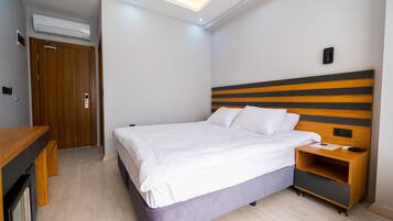 Quarto de hotel com cama, mesa de cabeceira e escrivaninha.