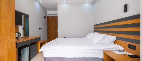 Quarto de hotel moderno com uma cama grande, cabeceira de madeira, mesas de cabeceira, televisão integrada e minibar.