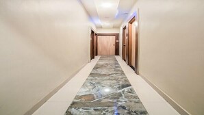 Um corredor com piso de mármore, portas de madeira e parede em tons claros.