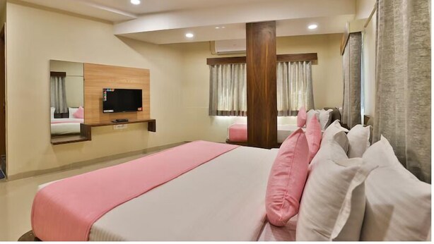 Quarto de hotel com uma cama grande, uma TV fixada na parede e uma janela com cortinas.