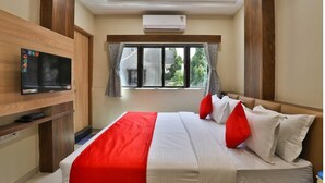 Quarto de hotel com cama, televisão, aparelho de ar condicionado e janela com cortinas.