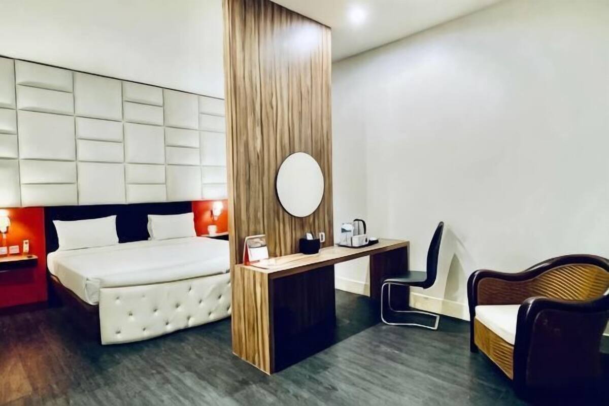 Quarto de hotel moderno com cama, escrivaninha, cadeira e um espelho grande.