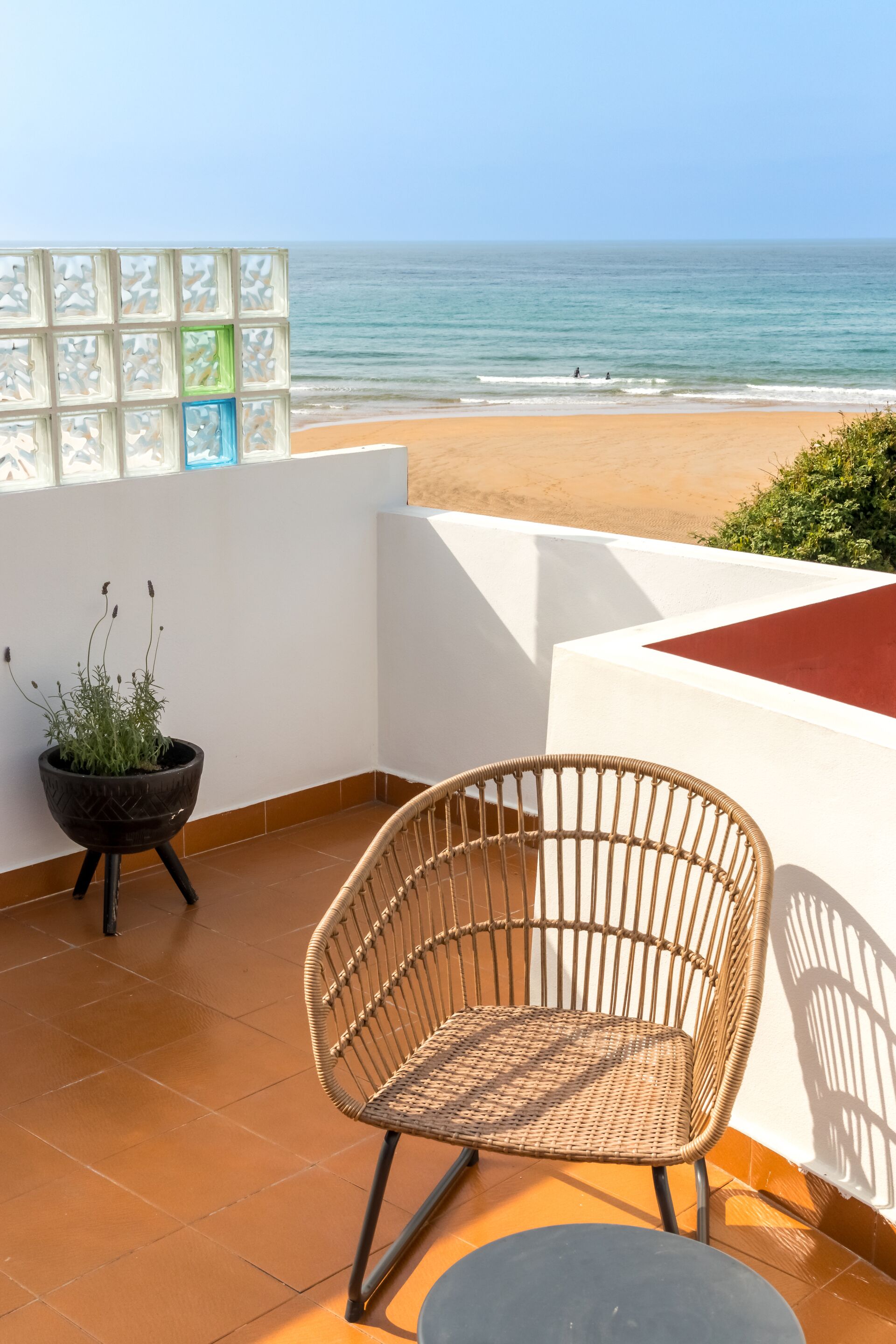 Uma varanda com cadeira de vime, planta em vaso e vista para a praia.